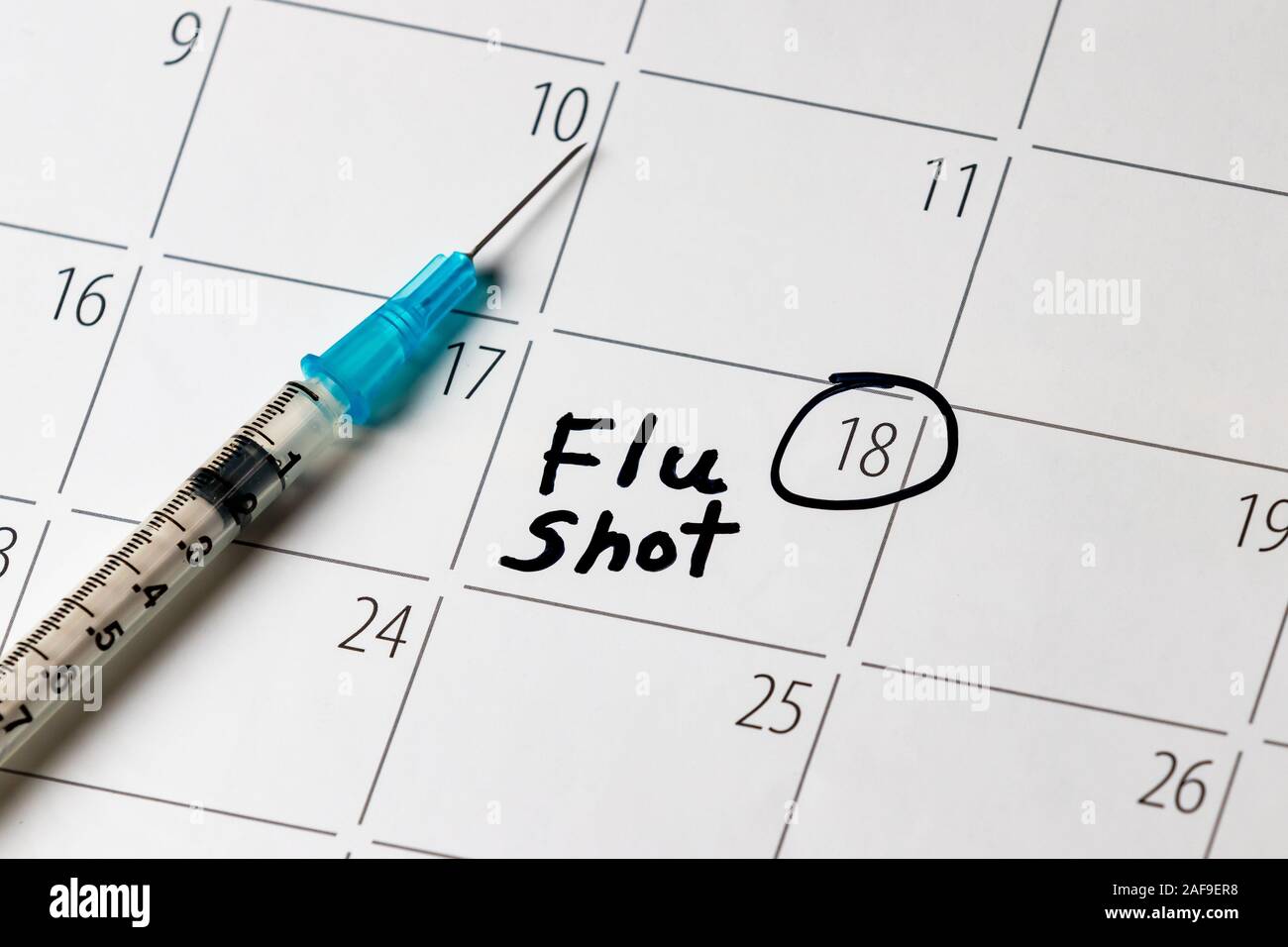 Flu shot reminder written in black ink on white calendar. Syringe with ...
