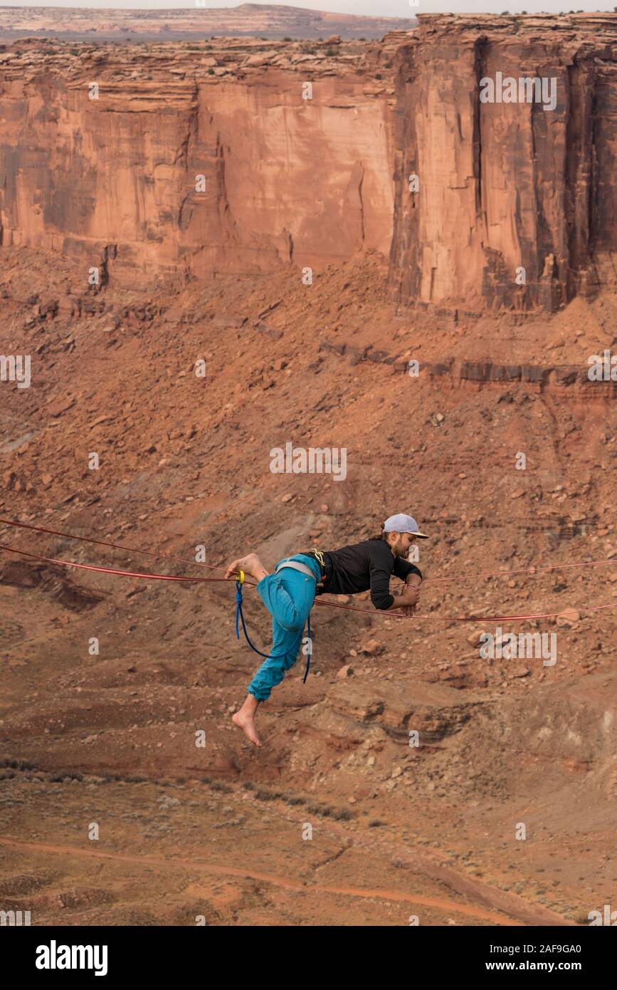 A young man takes a break to rest on the line while slacklining or ...