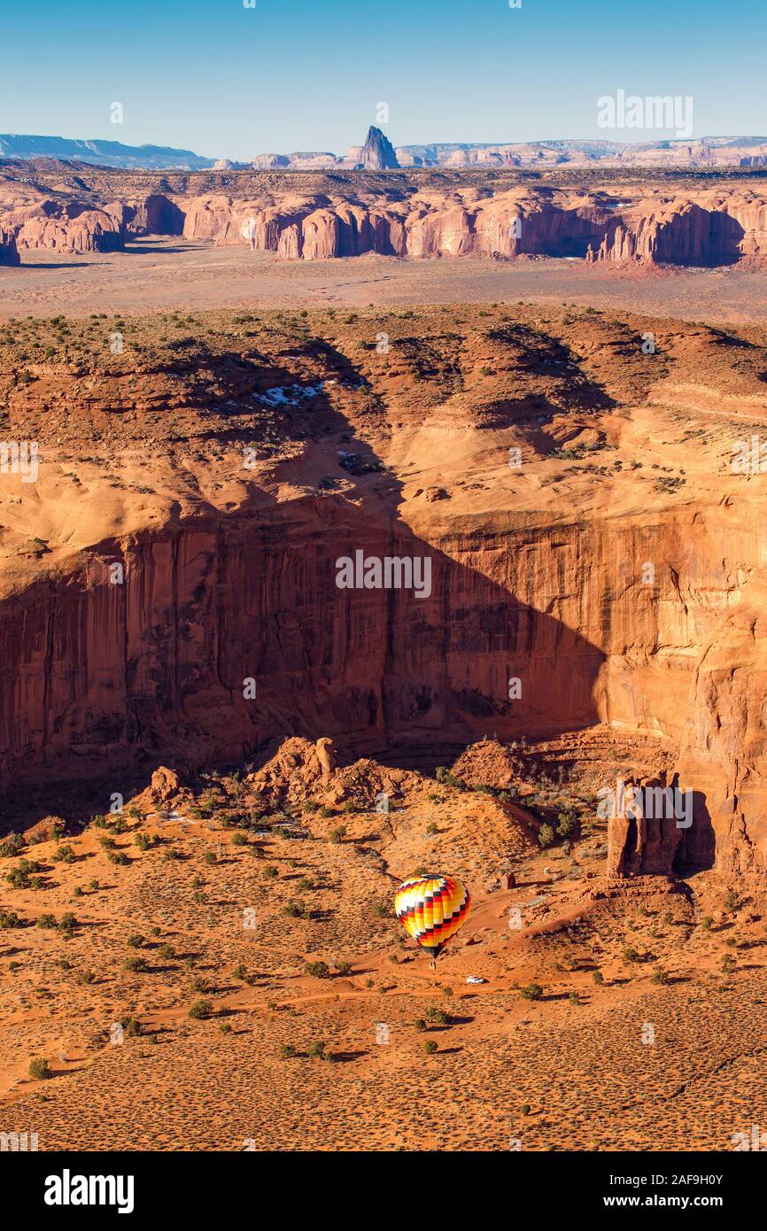 An aerial view of a hot air balloon flying in front of Rain God Mesa in ...