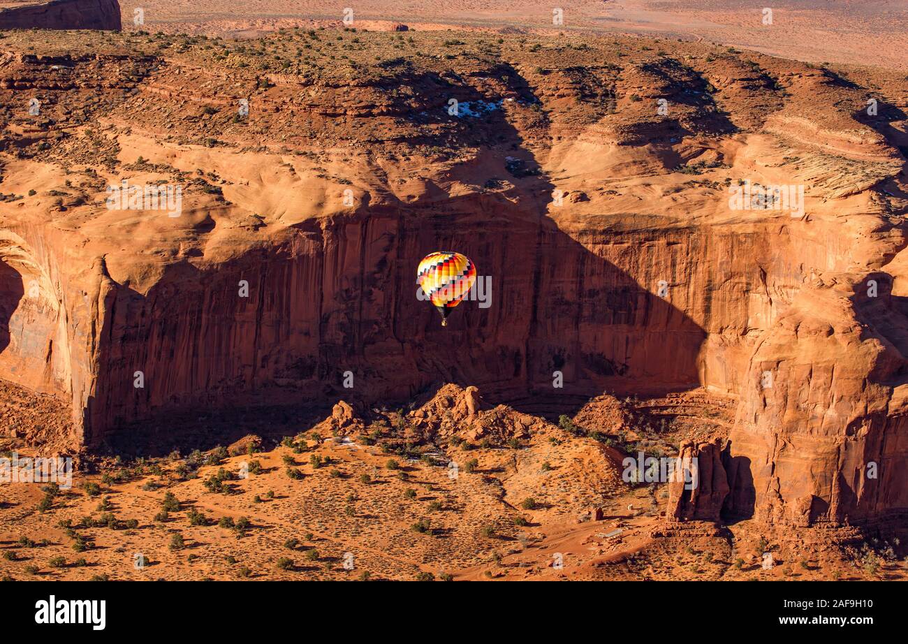 An aerial view of a hot air balloon flying in front of Rain God Mesa in ...