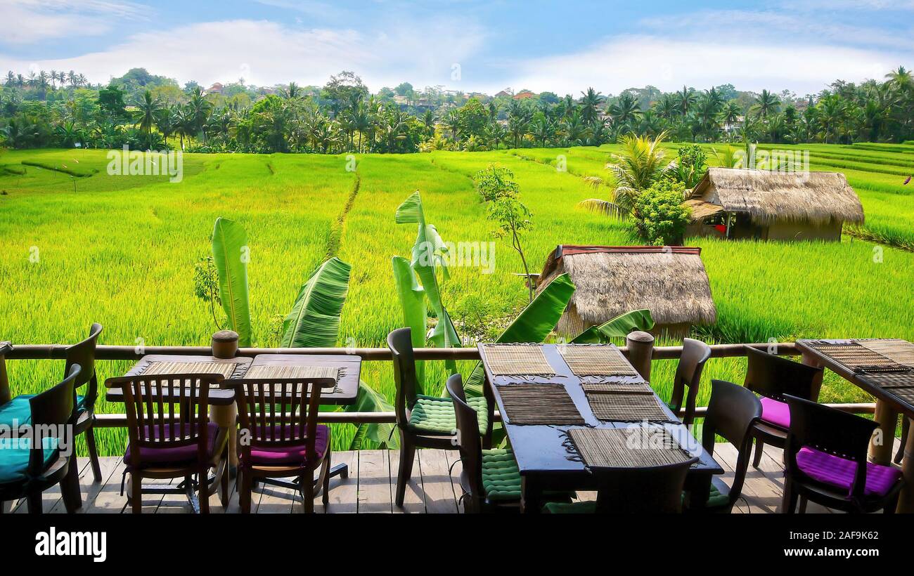 A rustic wooden deck with simple tables and chairs overlooking a rice ...