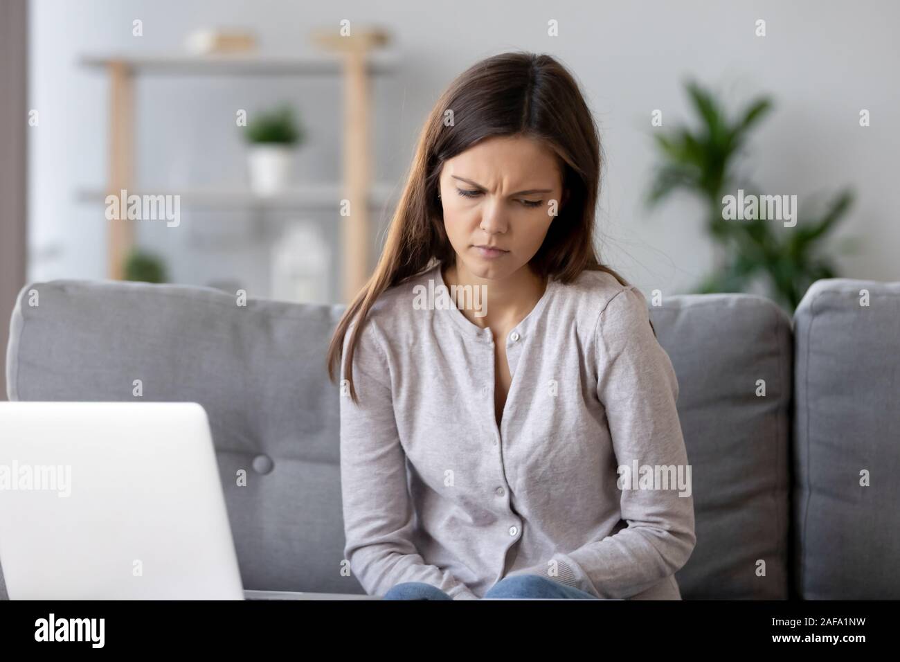 Pensive young woman sit on couch with laptop thinking Stock Photo - Alamy