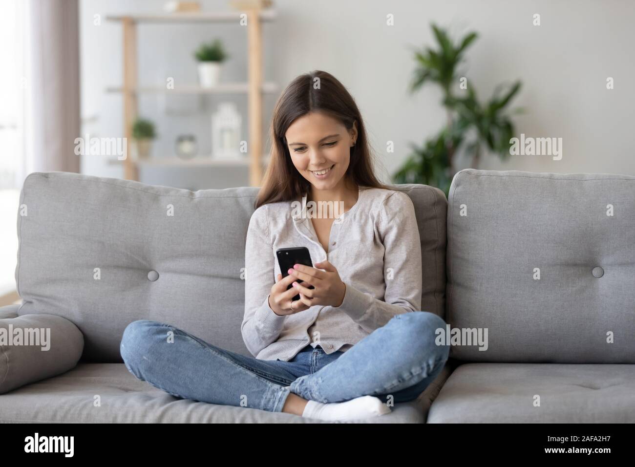 Smiling teenager sit on couch use smartphone texting message Stock ...