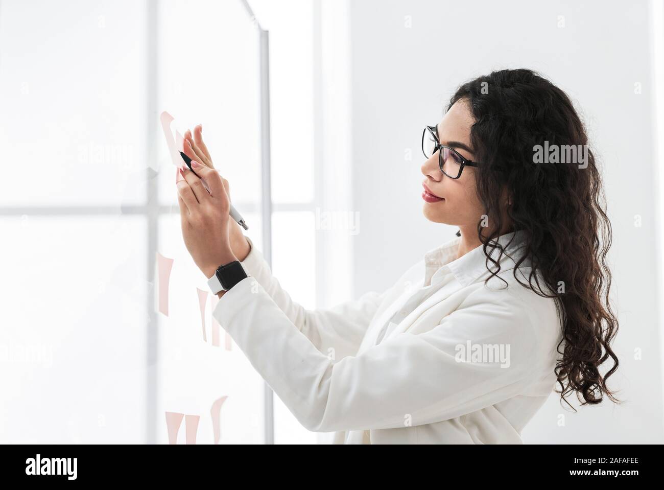 Hispanic manager putting sticky notes on glass wall Stock Photo - Alamy