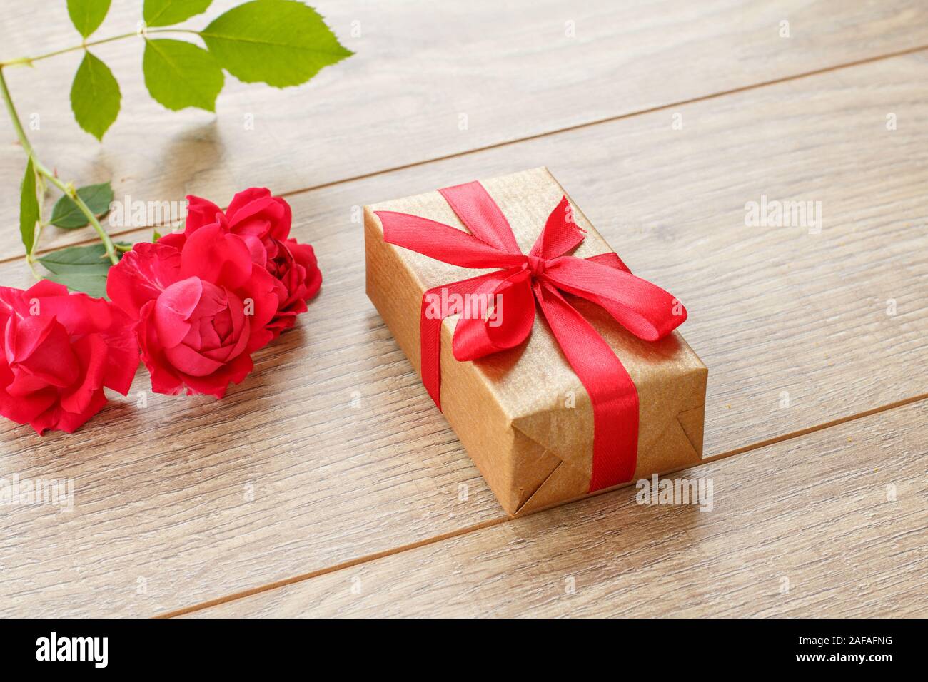 Gift box with red ribbon on wooden boards decorated with red rose ...
