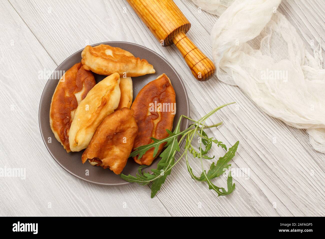 Plate with fried pies, greens and wooden rolling pin on table. Top view ...