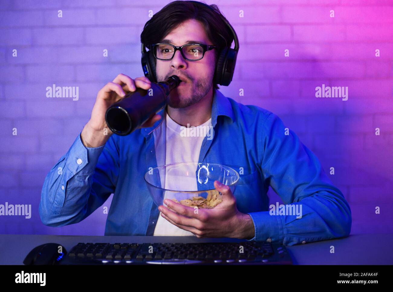 Concentrated gamer drinking beer with chips, looking at screen Stock ...