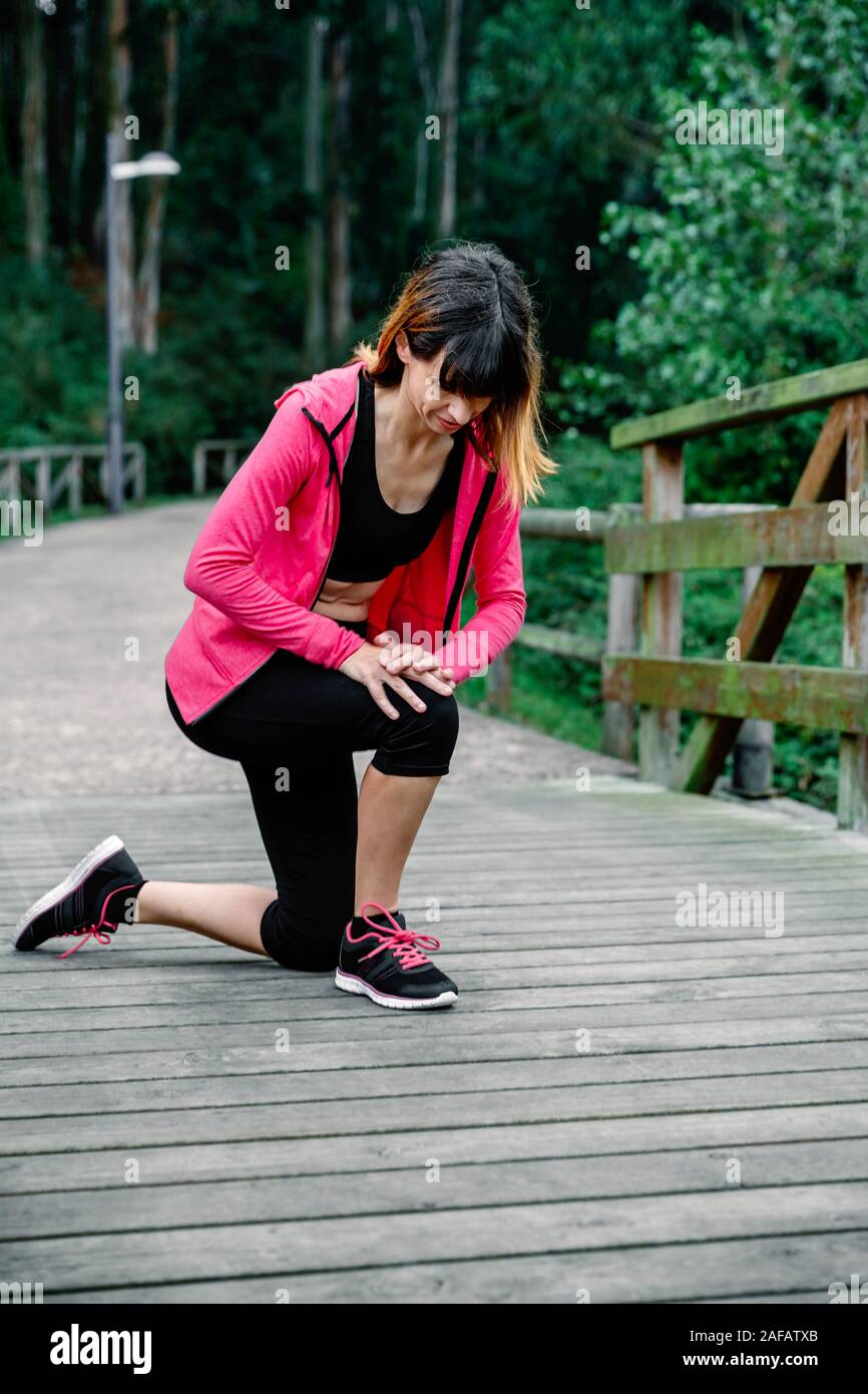 Athlete woman crouched with knee injury Stock Photo - Alamy