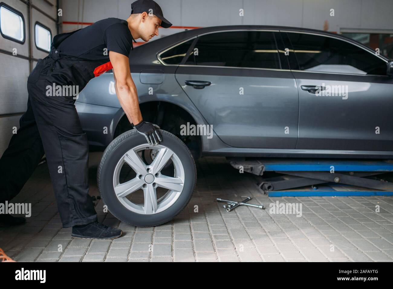 Auto mechanic in uniform holds wheel, tire service Stock Photo - Alamy