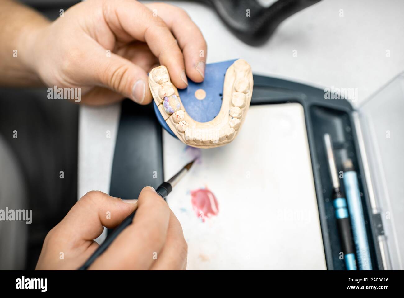 Dental technician coloring dental prosthesis with a paint brush at the ...