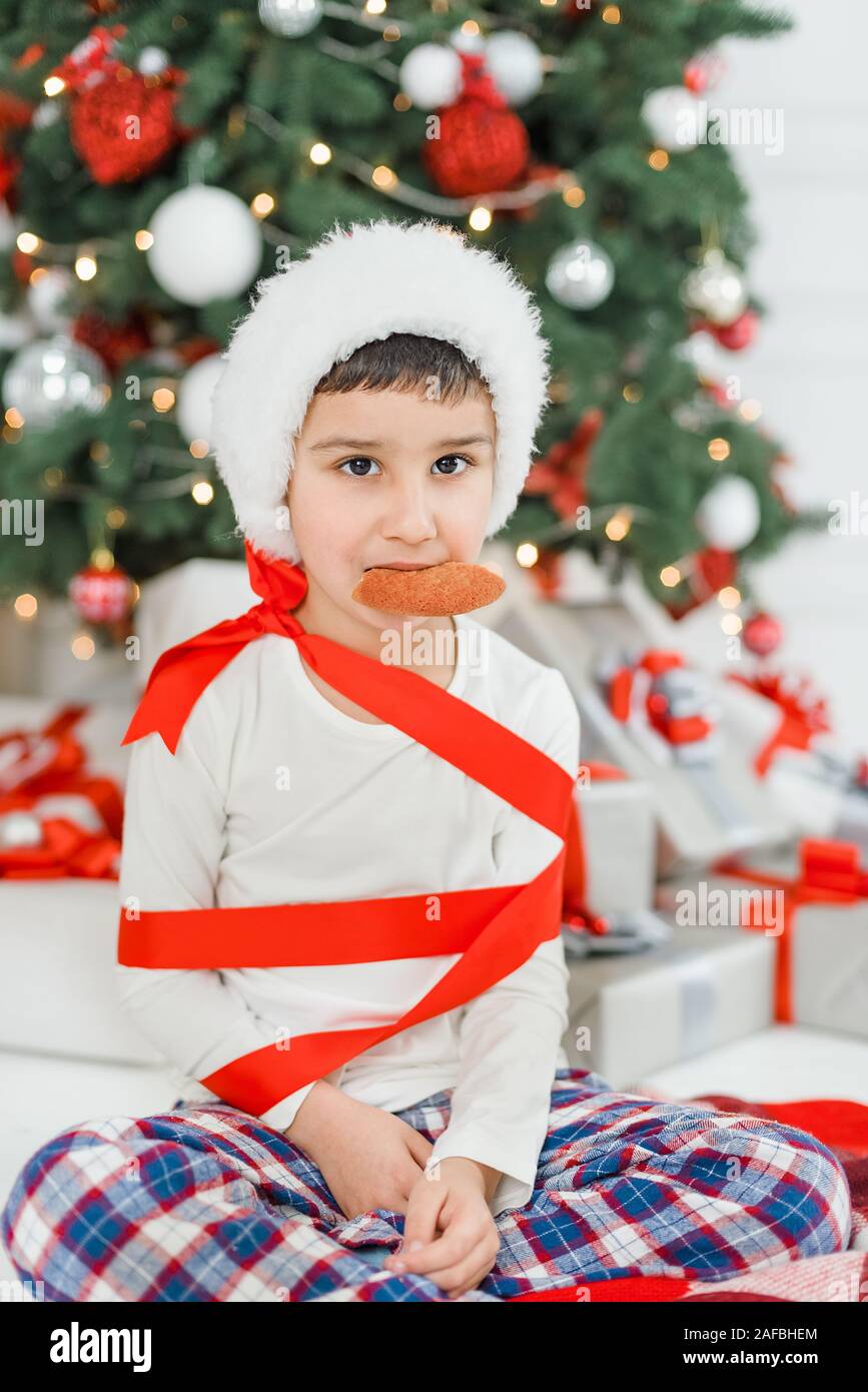 Disobedient child is bound with ribbon sitting under christmas tree ...