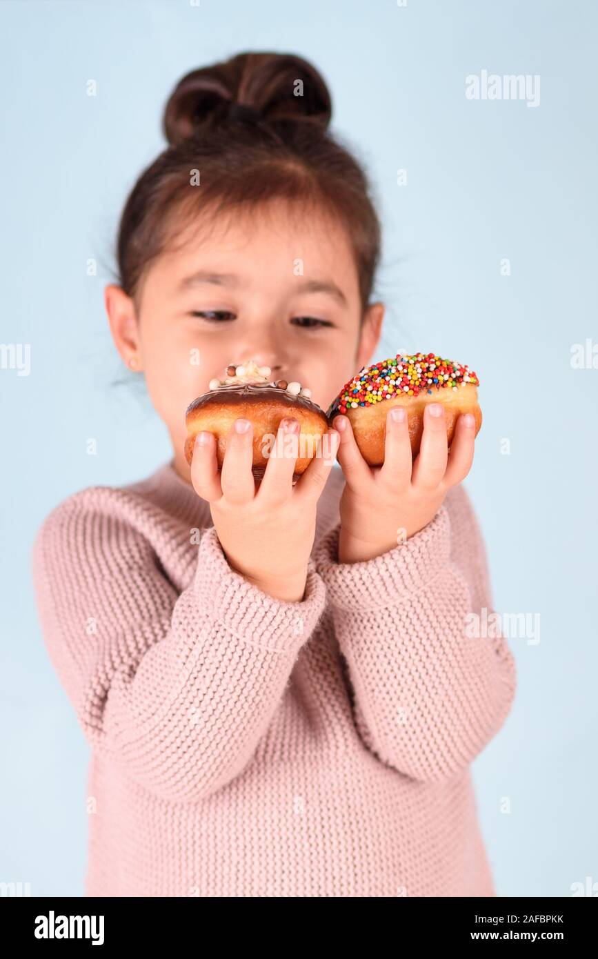 Little happy cute girl eating donuts on blue background. Child having ...