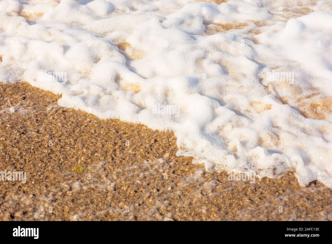 sea waves splash foam on the sunny beach. mess of salt water and sand ...