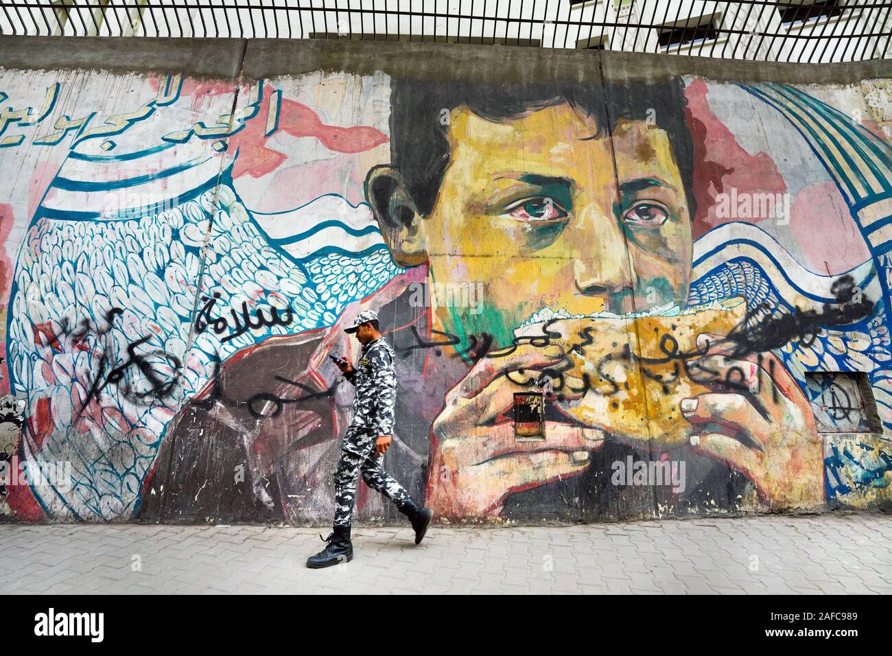 Soldier walks in front of a revolutionary mural on a wall of martyrs ...