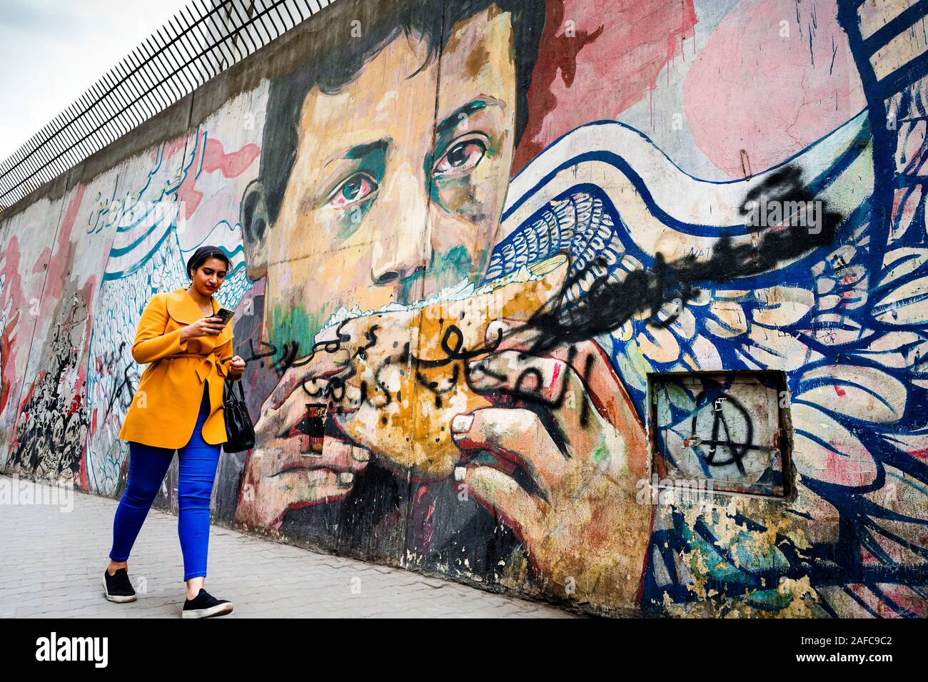 Woman walks in front of a revolutionary mural on a wall of martyrs near ...