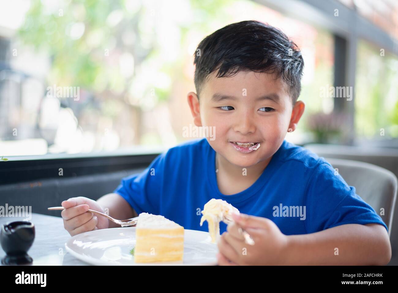 Cute little Asian boy eating cake in bakery shop or cafe Stock Photo ...