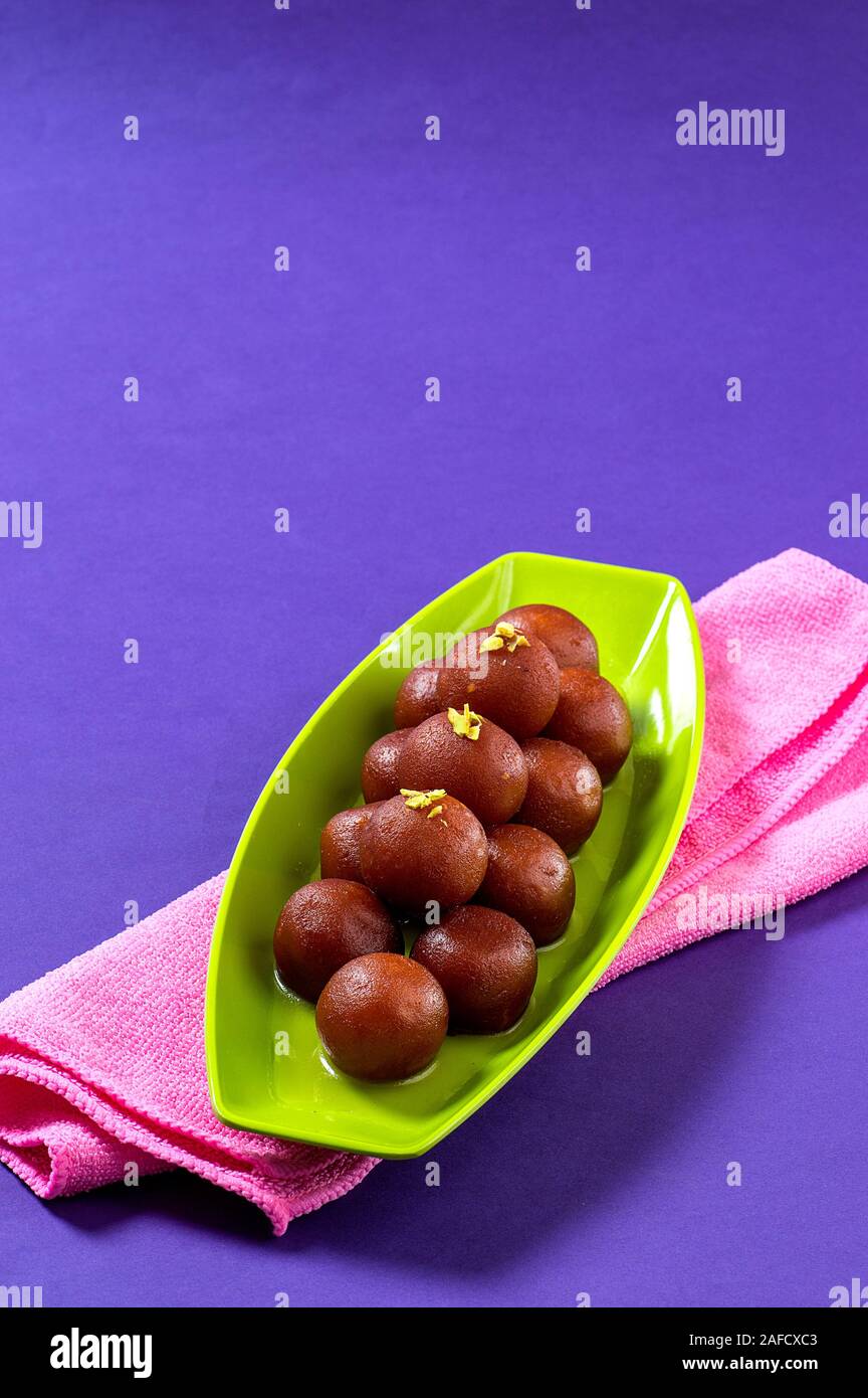 Indian Dessert Gulab Jamun in plate on purple background with napkin ...