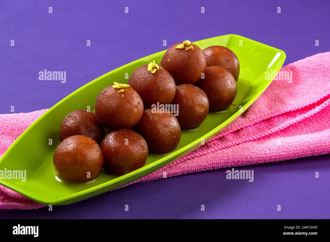 Indian Dessert Gulab Jamun in plate on purple background with napkin ...