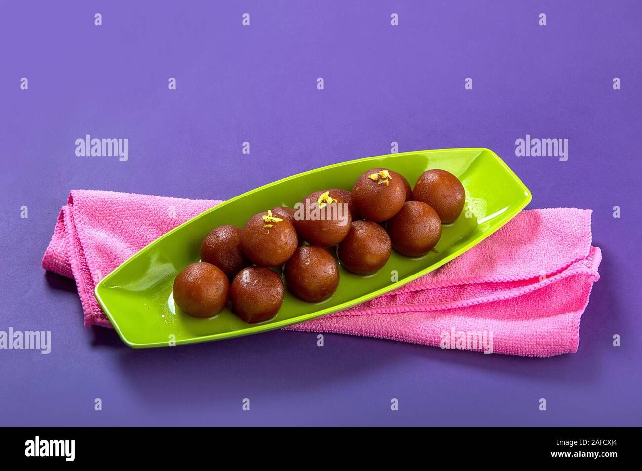 Indian Dessert Gulab Jamun in plate on purple background with napkin ...