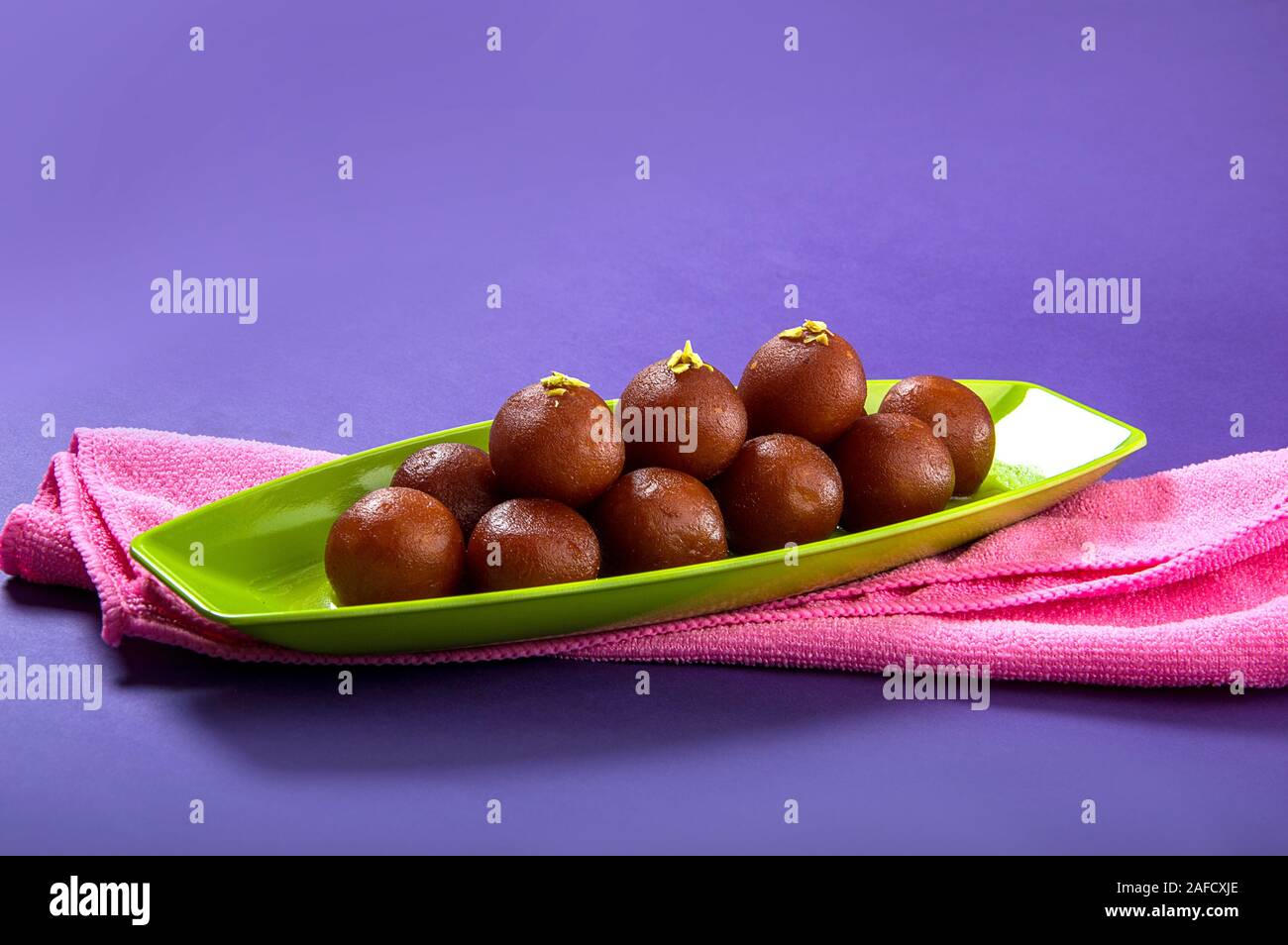 Indian Dessert Gulab Jamun in plate on purple background with napkin ...