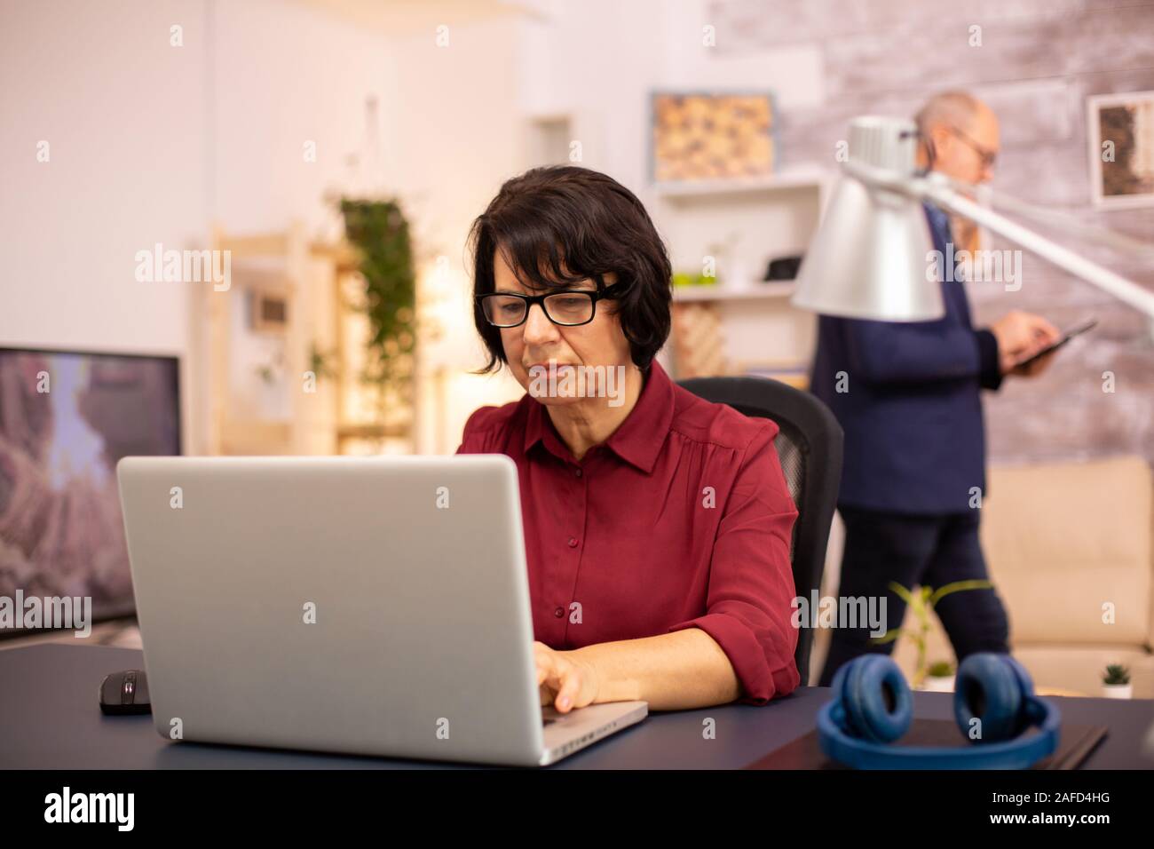 Old woman using a modern computer in her living room while her husband ...