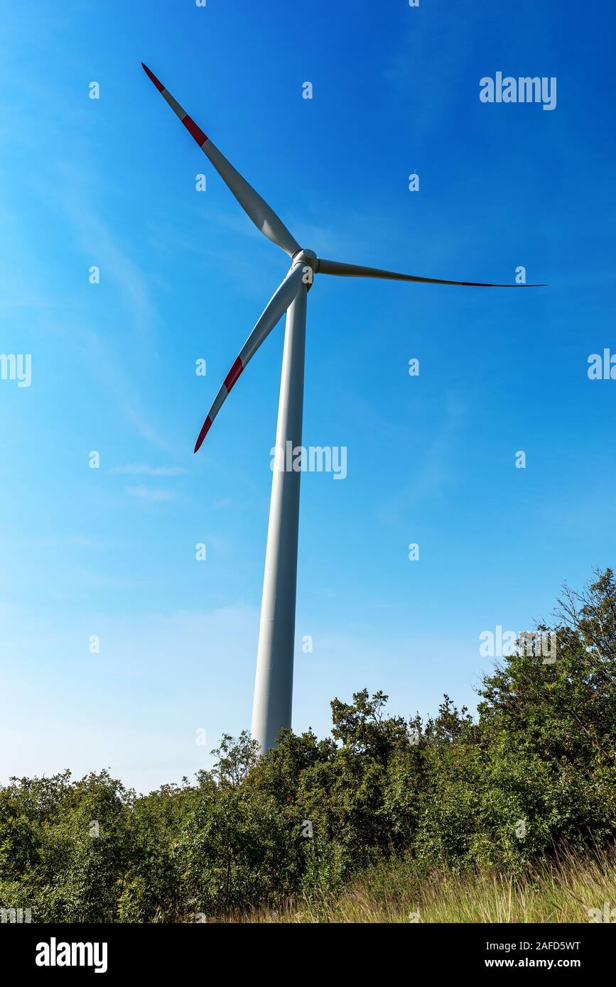 White and red wind turbine above a hill on a blue sky with clouds ...