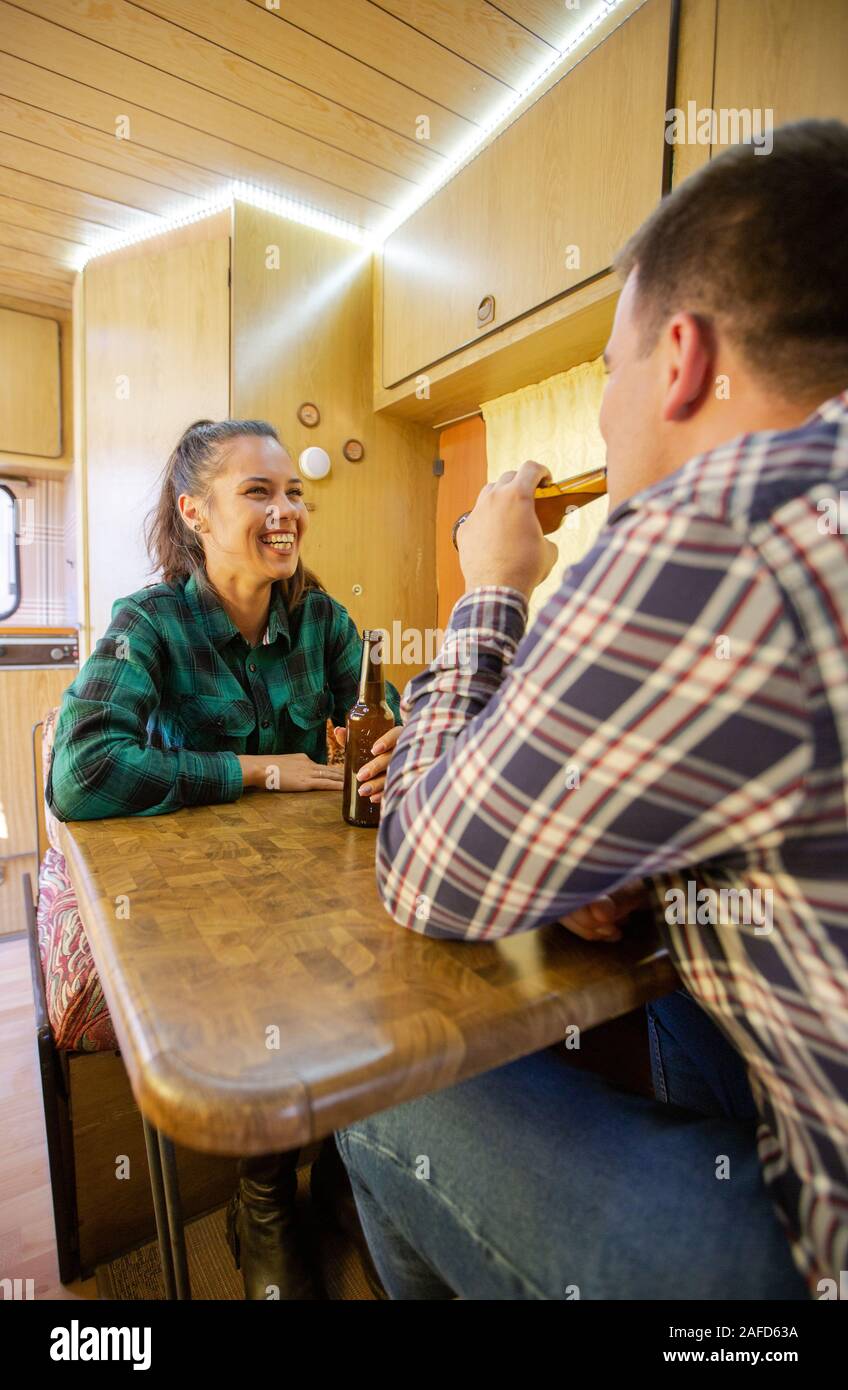 Loving couple smiling and chatting while drinking beer in the caravan ...