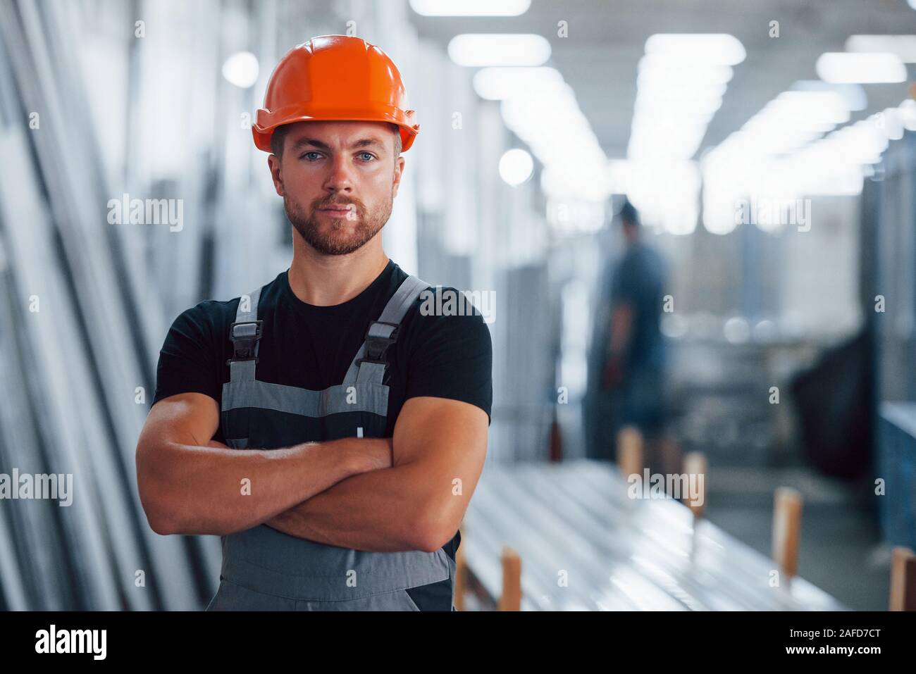 Stands with arms crossed. Portrait of male industrial worker indoors in ...