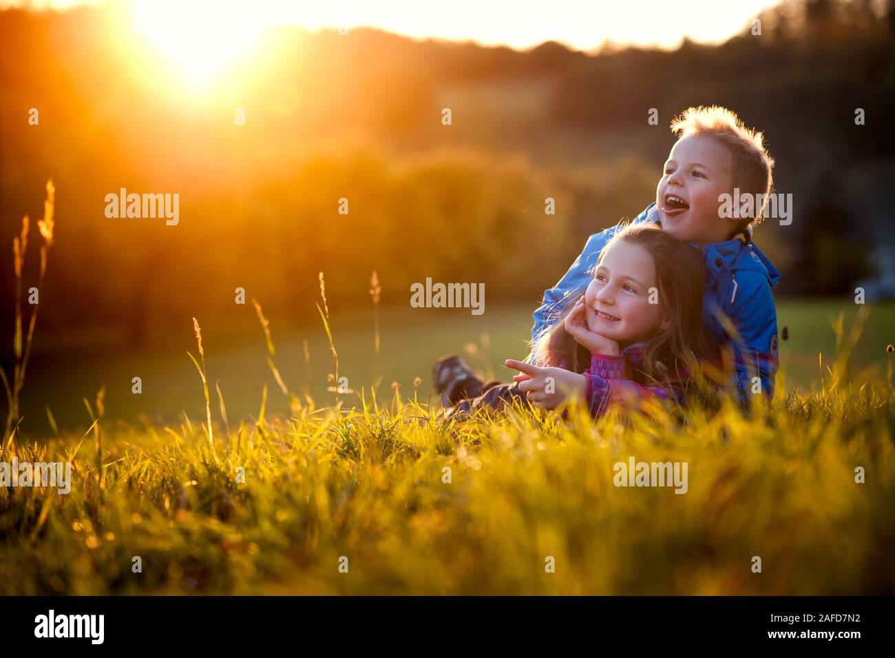 siblings sitting on a meadow at sunset Stock Photo - Alamy