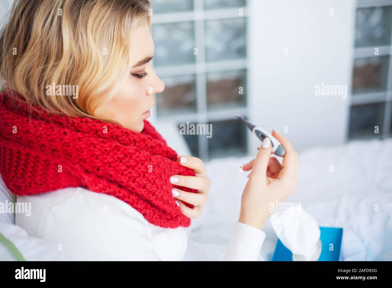 High temperature. Young woman looking at thermometer while holding it ...