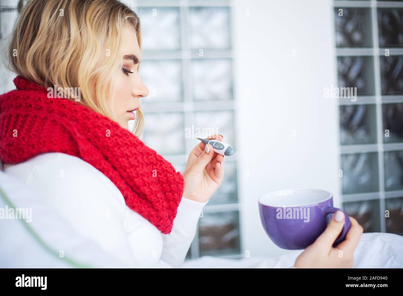 High temperature. Young woman looking at thermometer while holding it ...