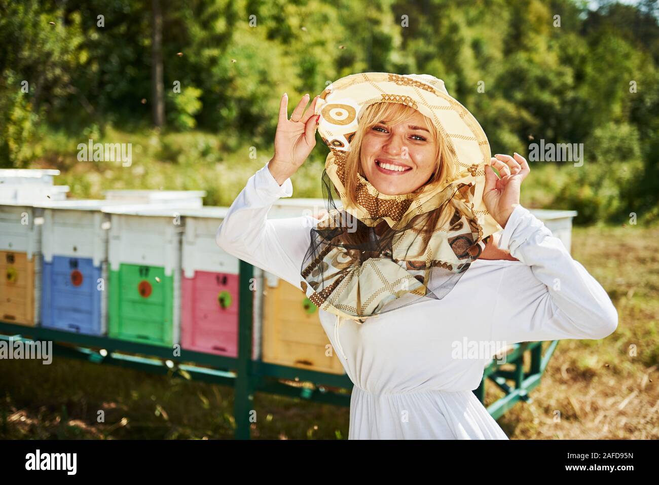 Female beekeeper stands against hives outdoors at sunny day Stock Photo ...