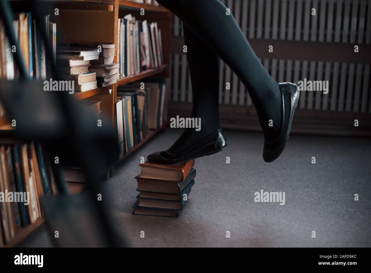 Standing on books and trying to reach top of shelves. Female student is ...