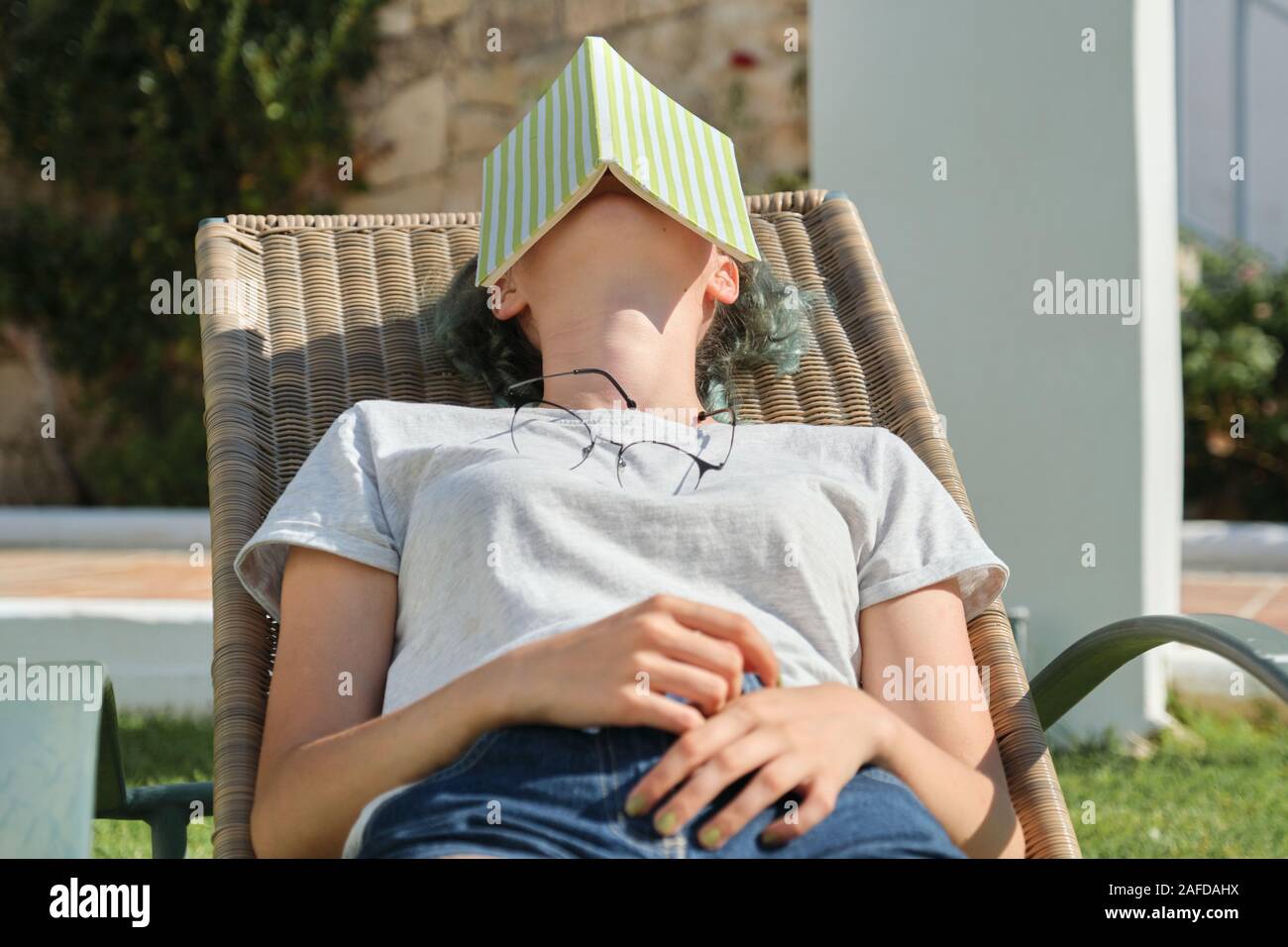 Teen girl resting outdoor sitting in chair, reading book and sleeping ...