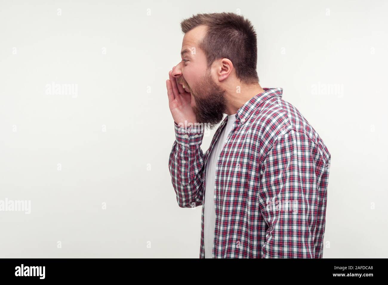 Side view of angry bearded man in casual shirt yelling loudly holding ...