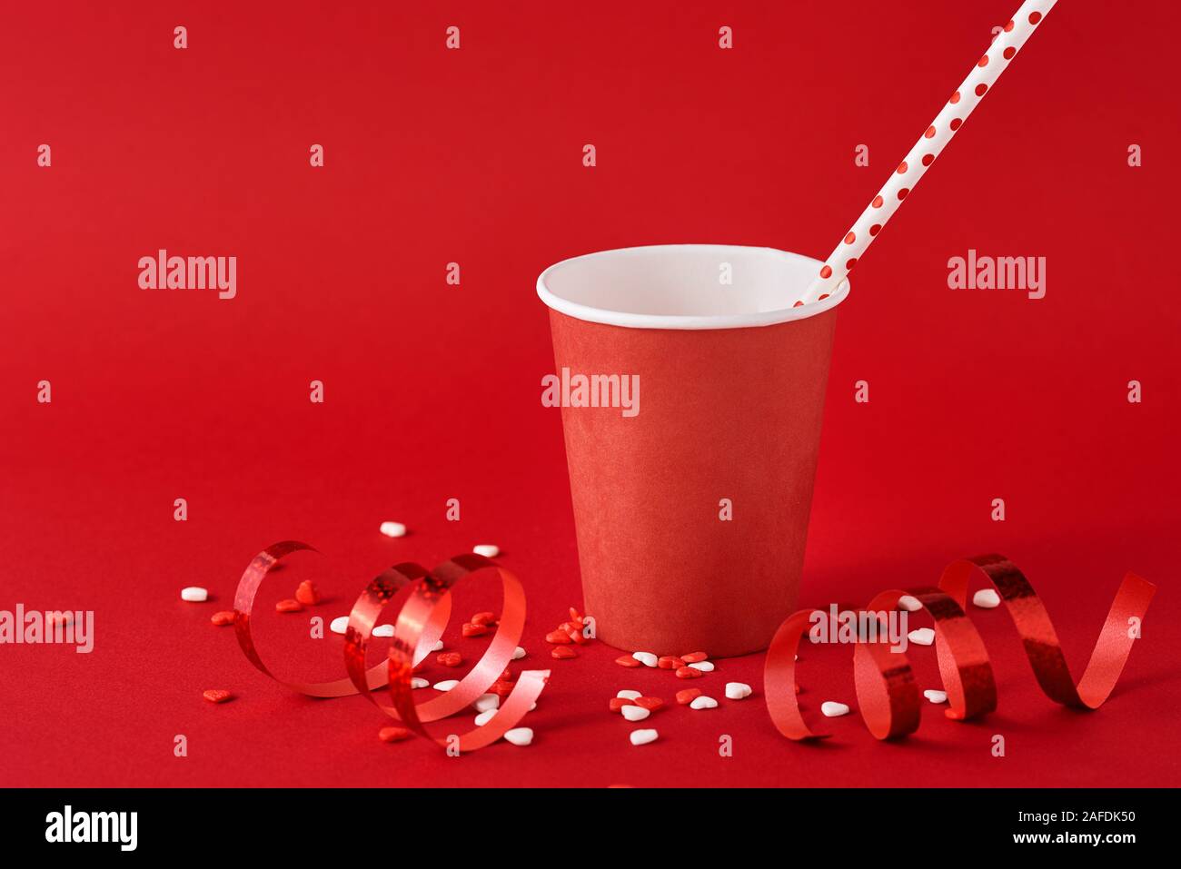 Paper coffee cup with festive decorations and confetti on red backgrond ...