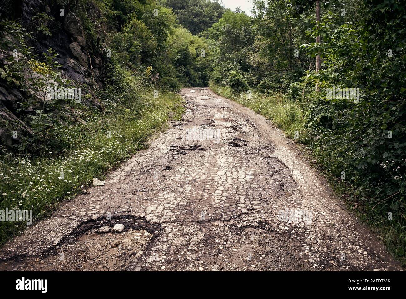 Countryside highly damaged road with many potholes and cracked asphalt ...