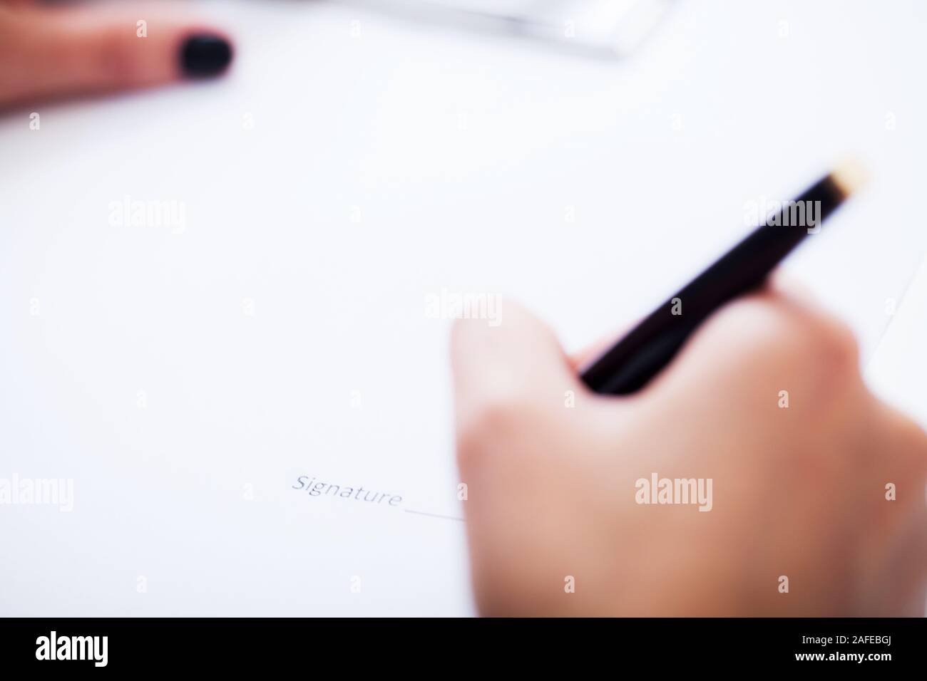 Close up girl hand putting signature on document. She situating at desk ...