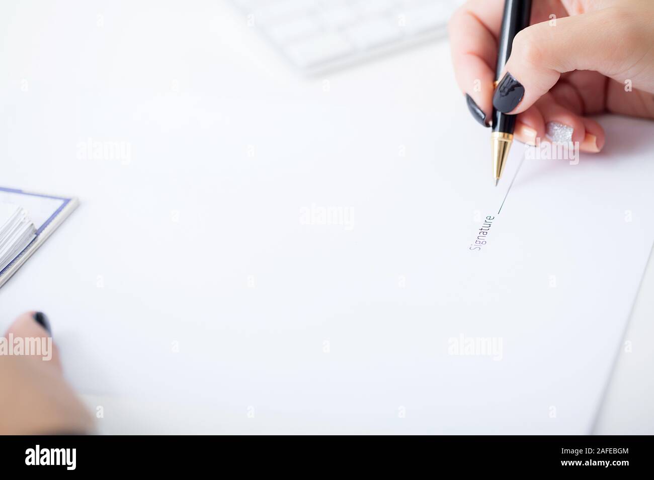 Close up girl hand putting signature on document. She situating at desk ...
