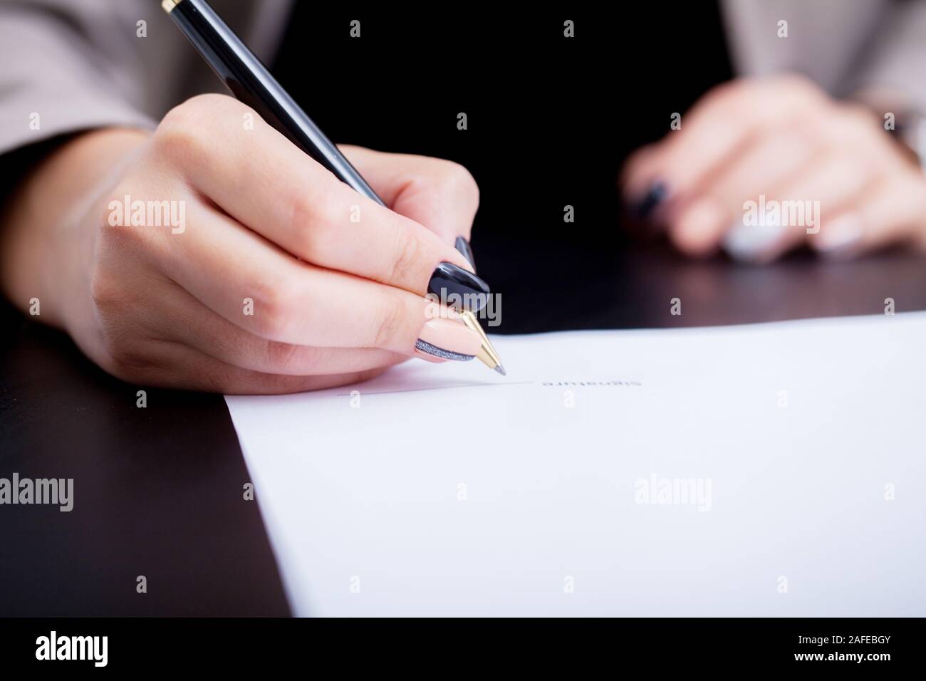 Close up girl hand putting signature on document. She situating at desk ...
