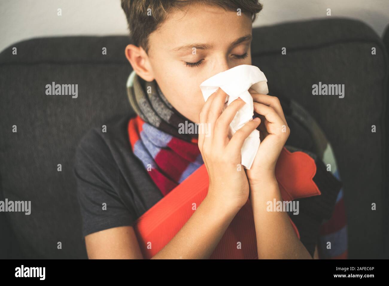 Sick boy with cold rhinitis sits with woolen blanket and hot water ...
