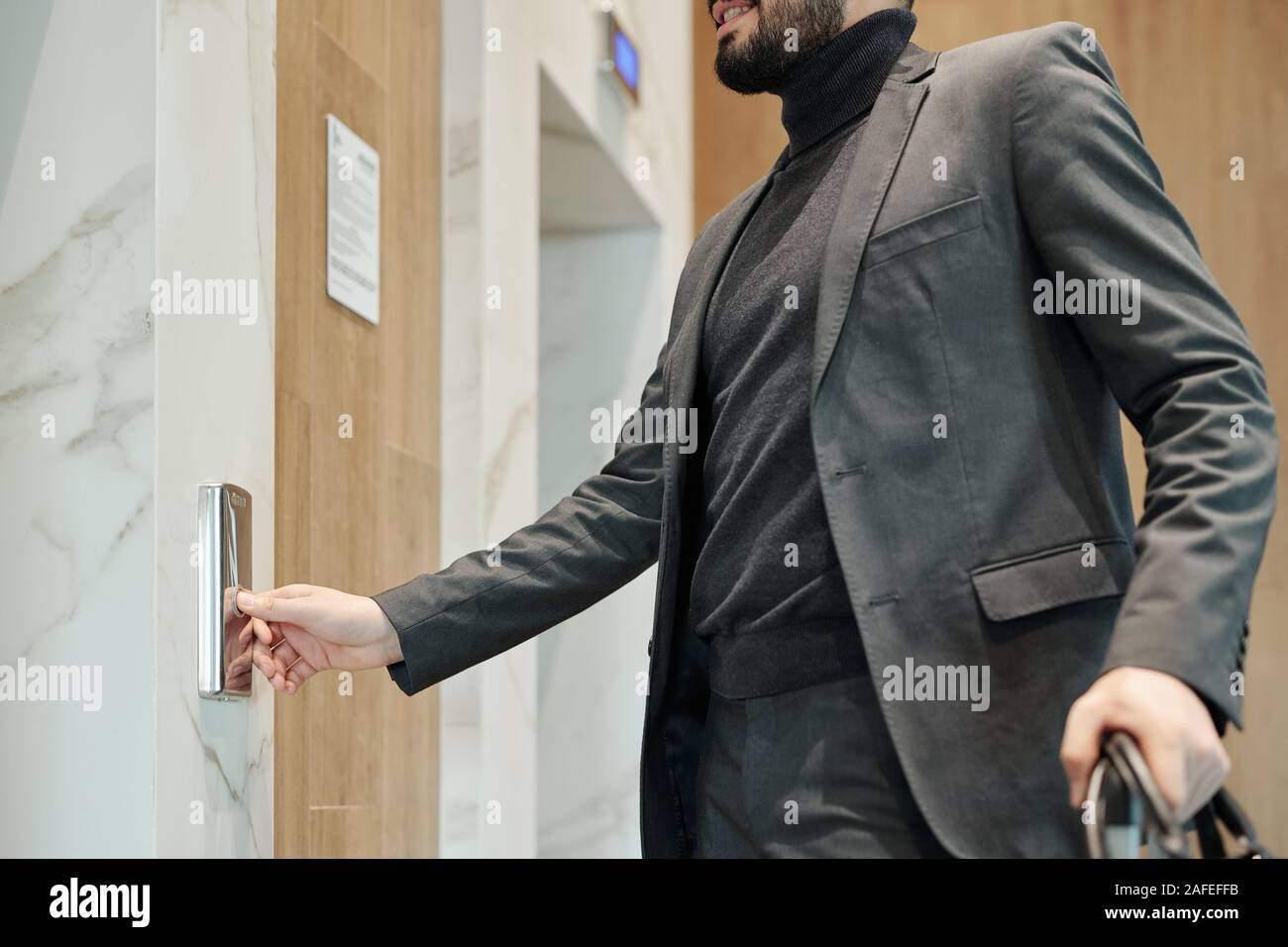 Young elegant businessman pushing button on the wall while waiting for ...