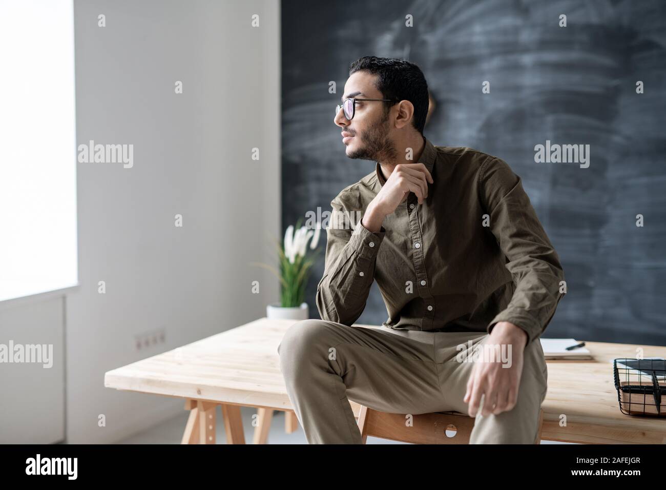 Restful male employee in eyeglasses and casualwear looking through ...