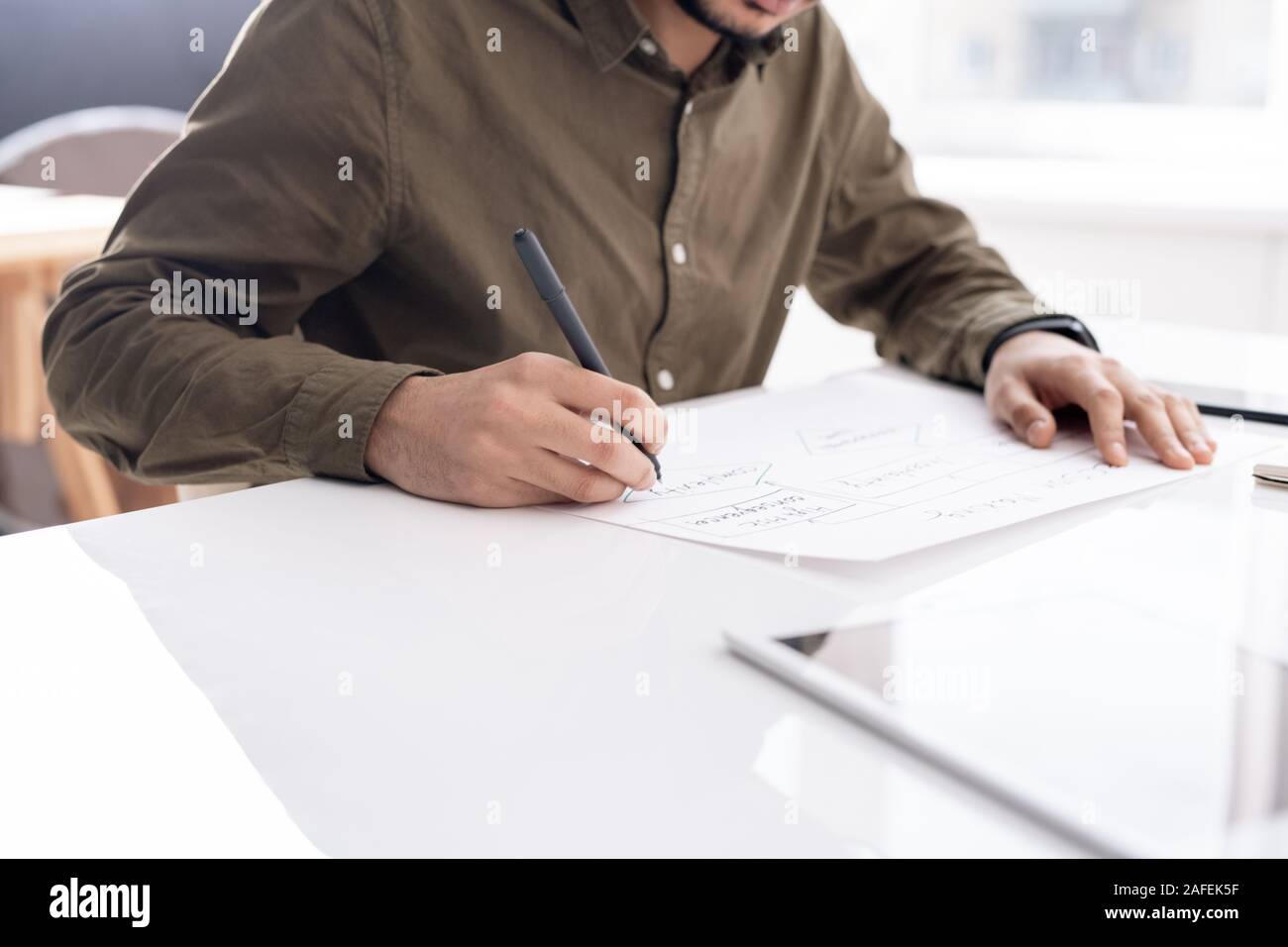 Young busy economist drawing flow chart on paper while preparing report ...