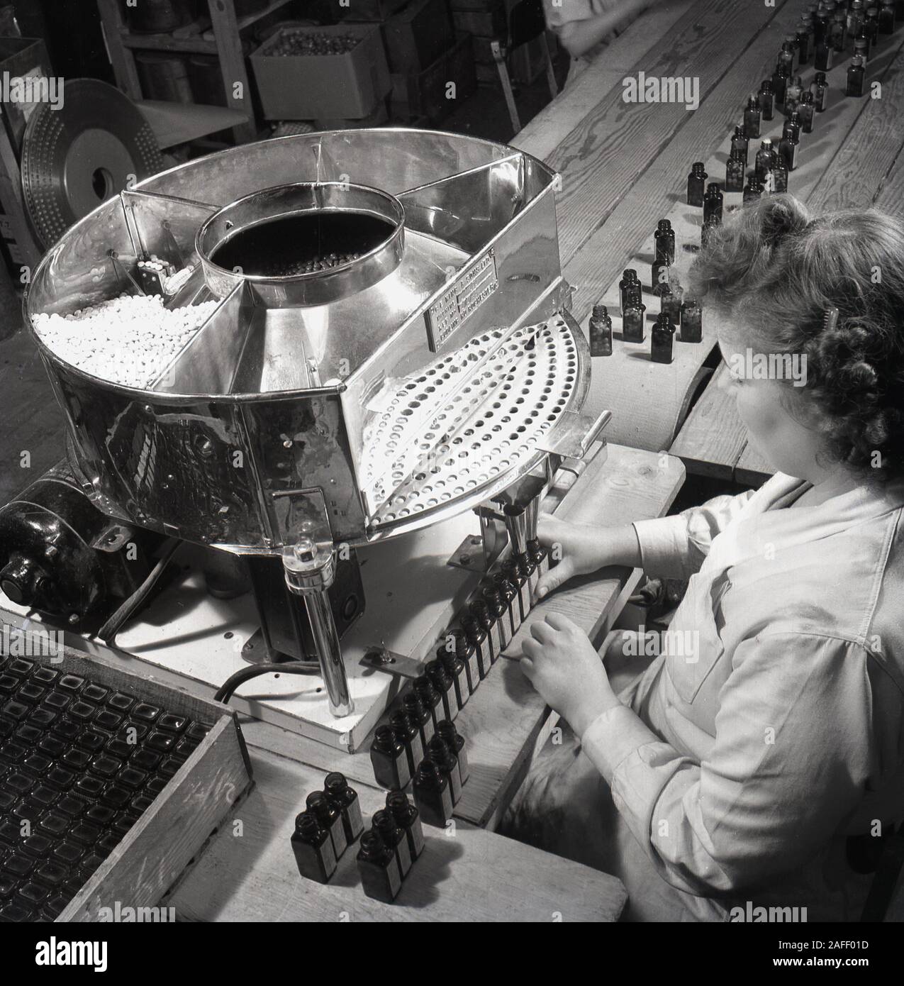 1950s, historical, a female worker sitting using a machine to put ...