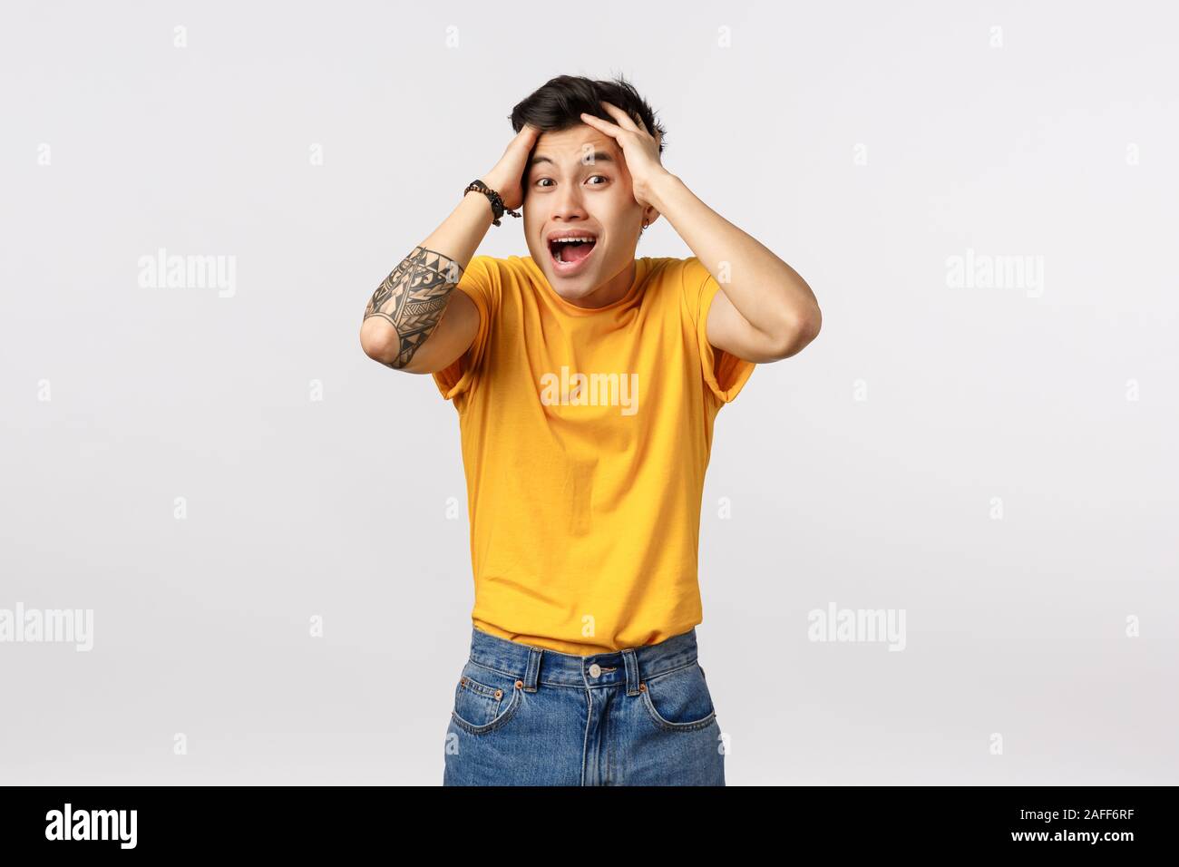 Scared attractive asian man with tattoos, wear yellow t-shirt ...