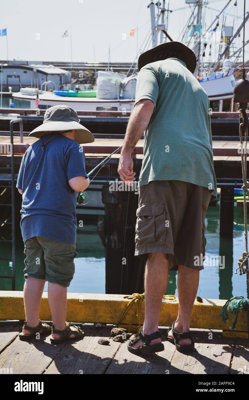 A man assists a boy with his fishing rod and reel from a pier at the ...