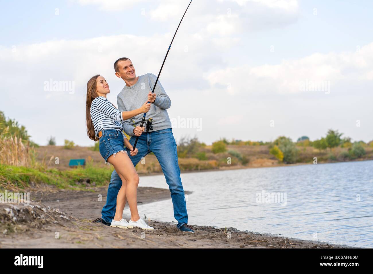 Happy young couple fishing by lakeside Stock Photo - Alamy