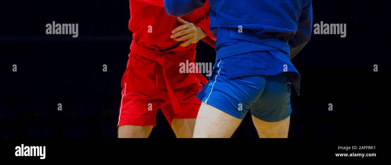 Two men in blue and red sambo wrestling on a yellow wrestling carpet in ...