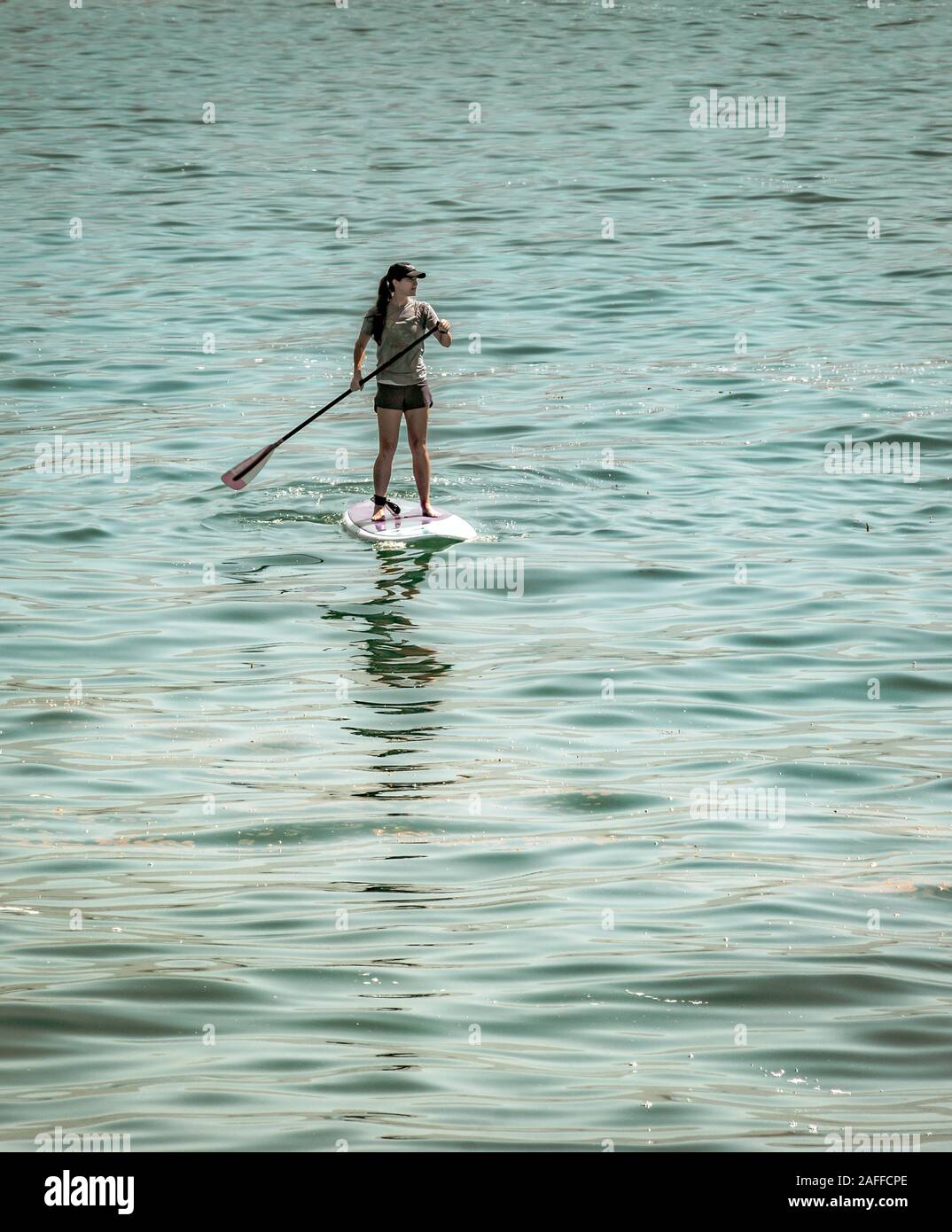 An isolated lone young woman paddles her Stand Up Paddleboard across ...